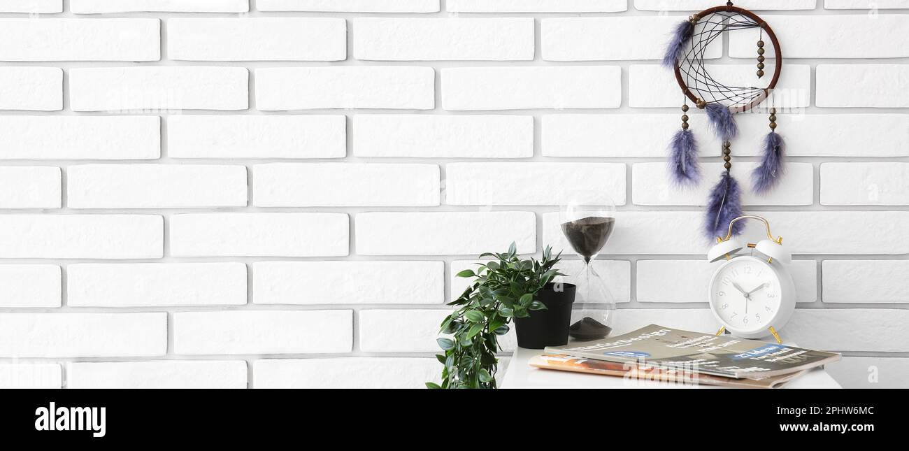 Stylish dream catcher hanging on light brick wall and table with alarm ...