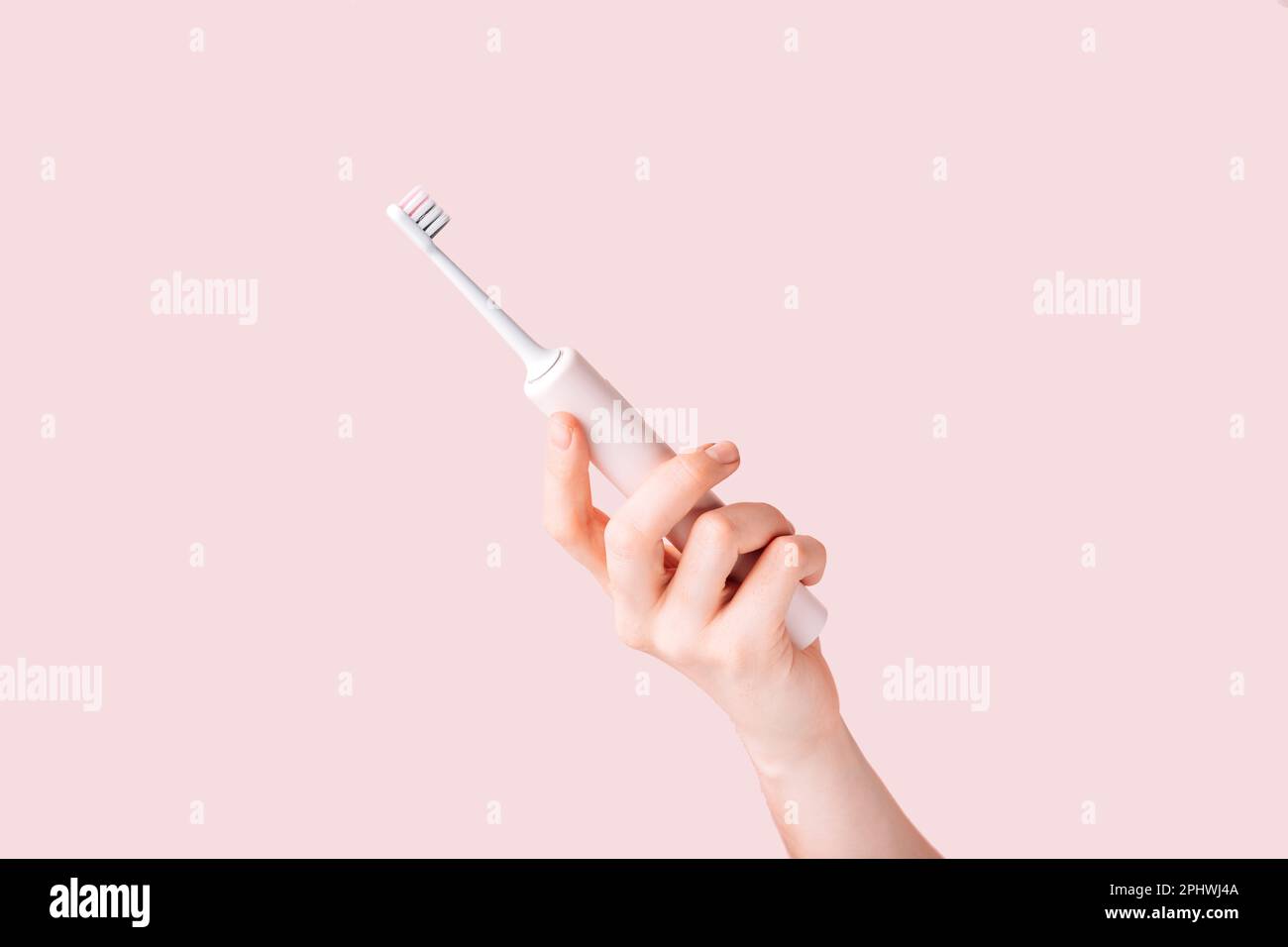 Electric toothbrush of pink color in female hand against pink ...