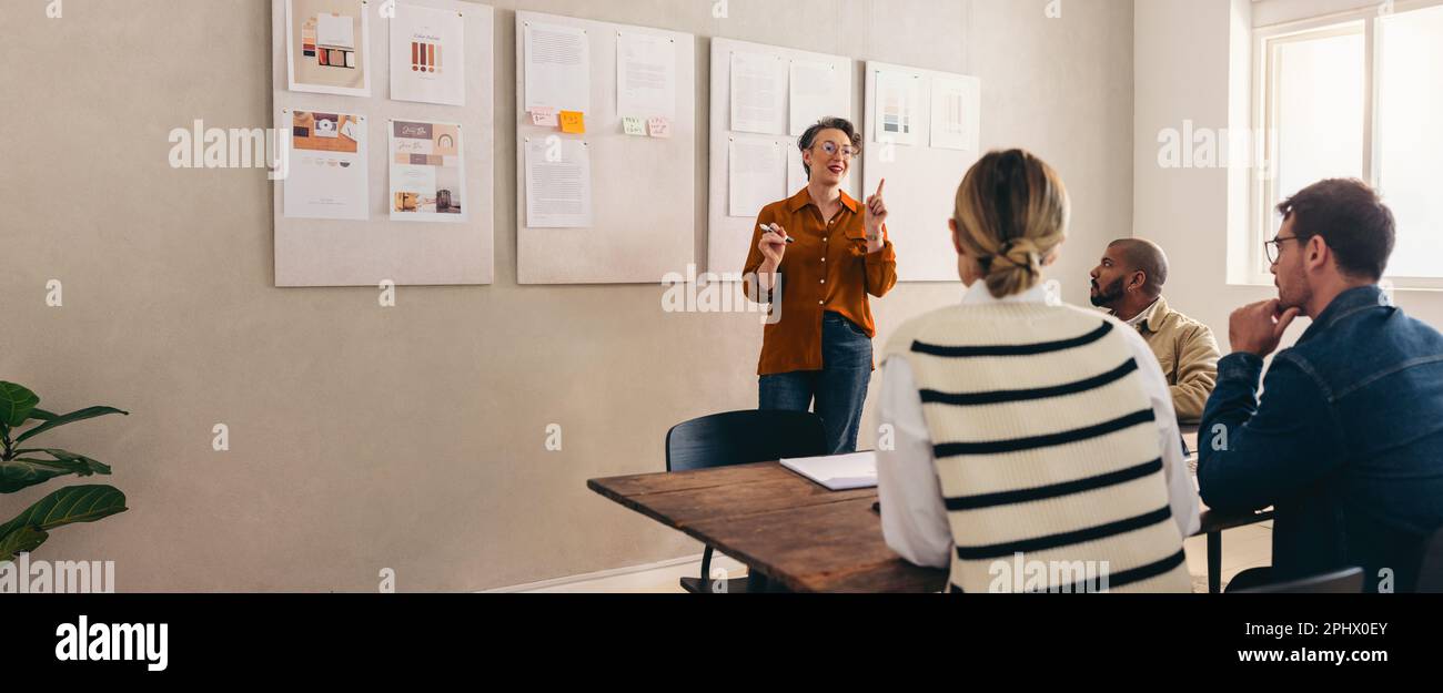 Mature designer pitching her idea to her team during a meeting. Mature ...