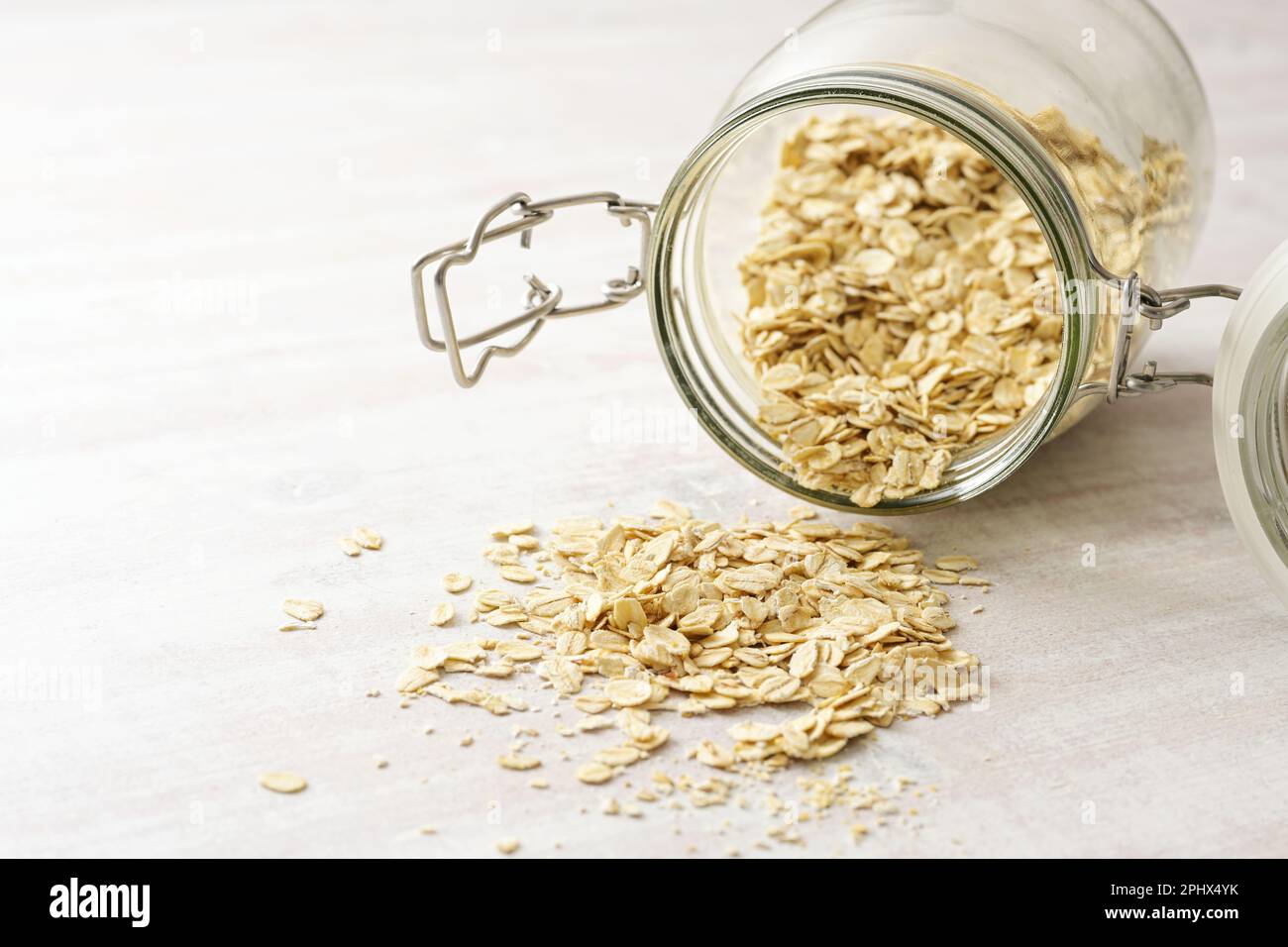 Oat flakes falling from a glass jar onto a light wooden table, healthy ...