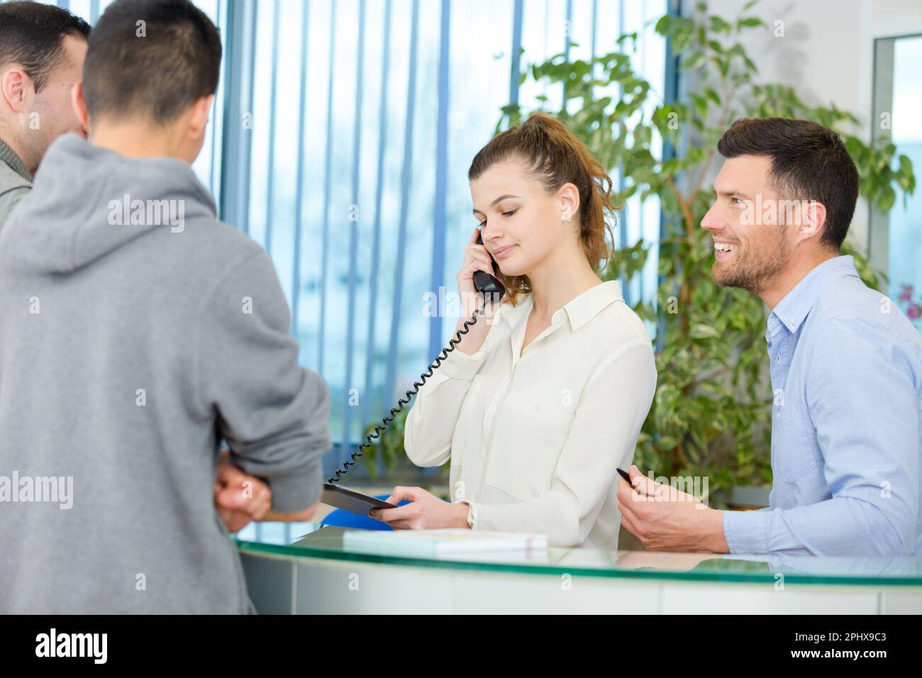 people waiting around reception desk while woman is on telephone Stock ...