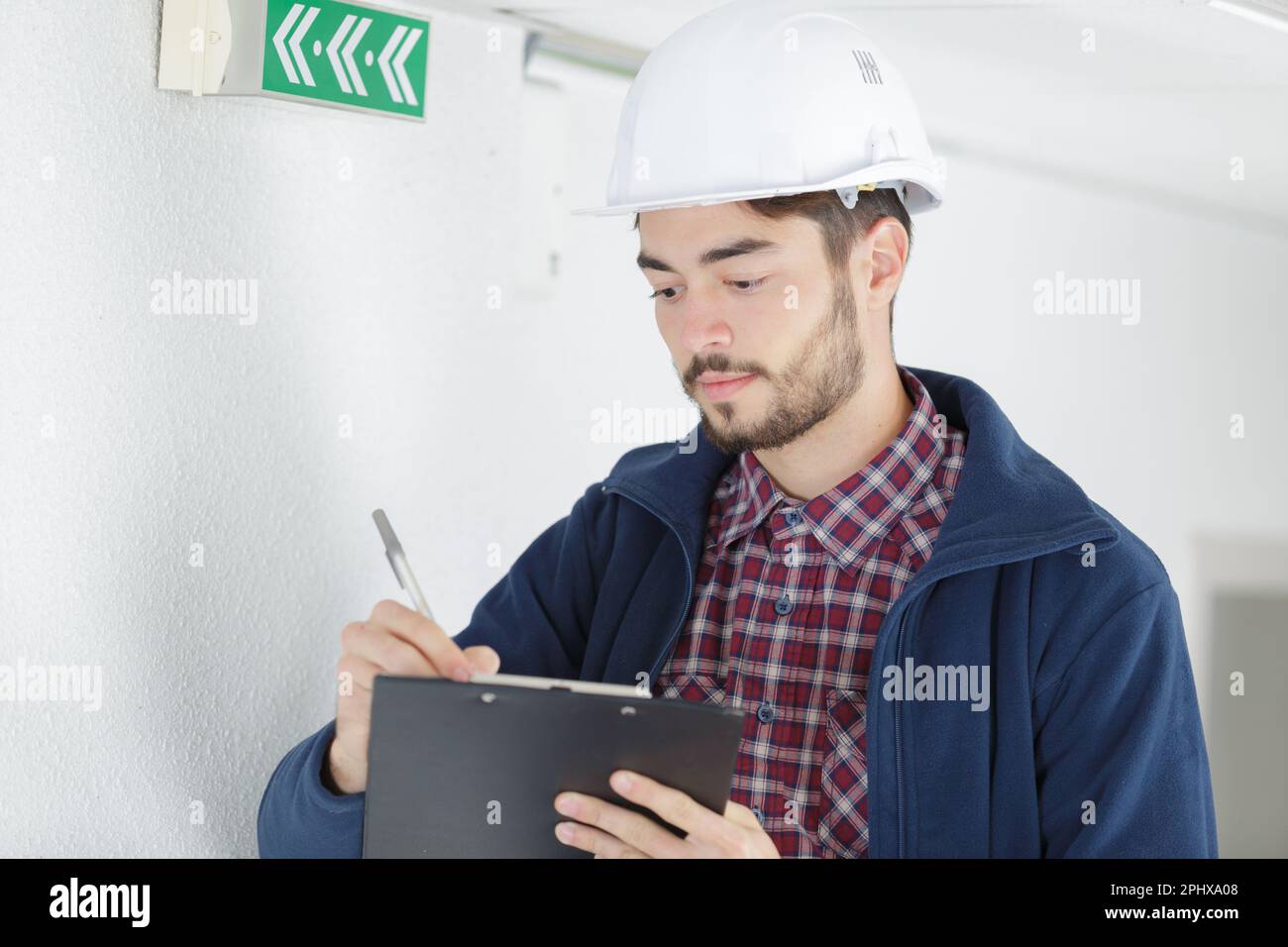 inspector next to fire escape sign making notes on clipboard Stock ...