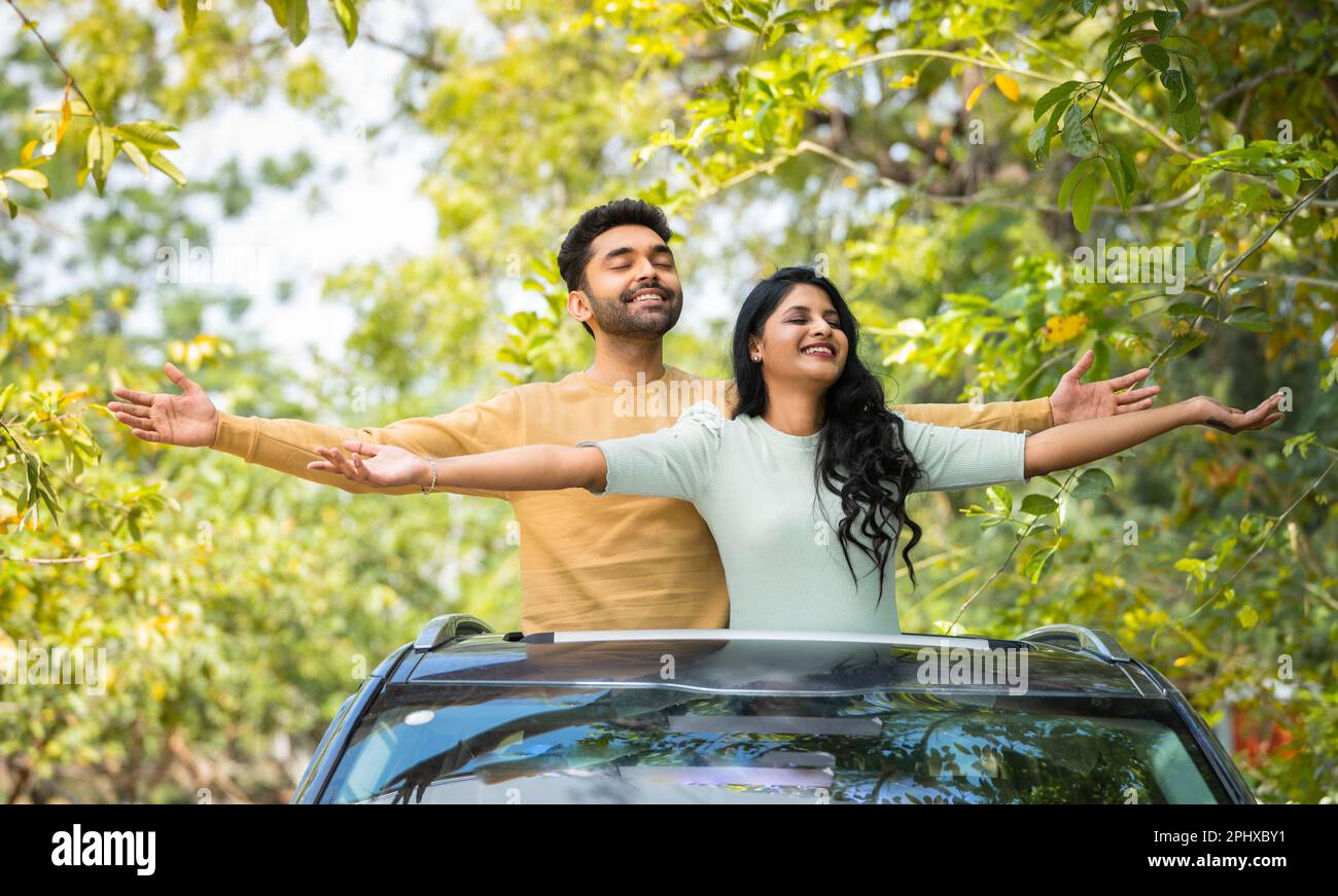Happy smiling couple feeling nature fresh air by stretching arms on car ...