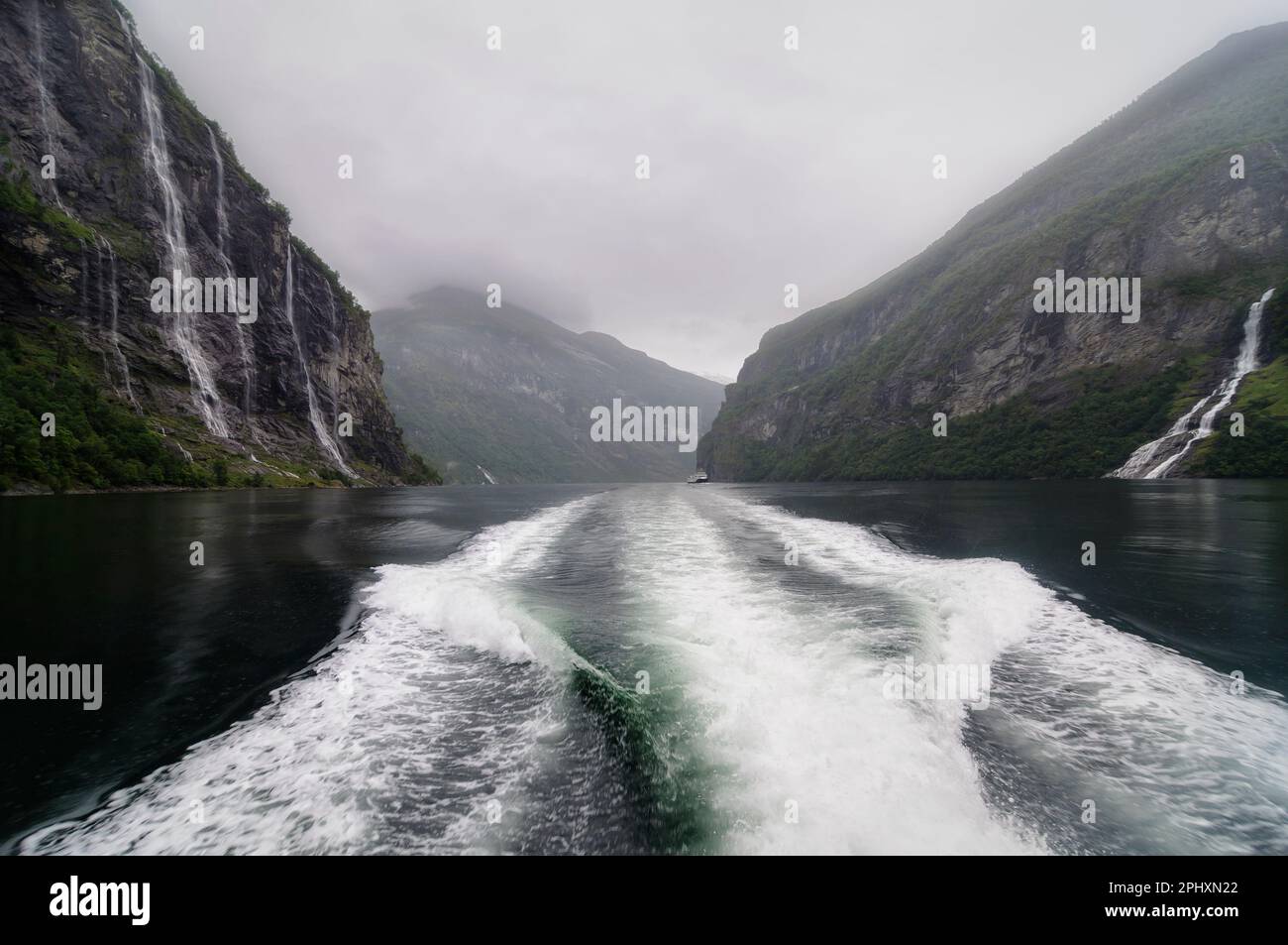 boat sailing in a fiord in Norway with waterfalls falling down the ...