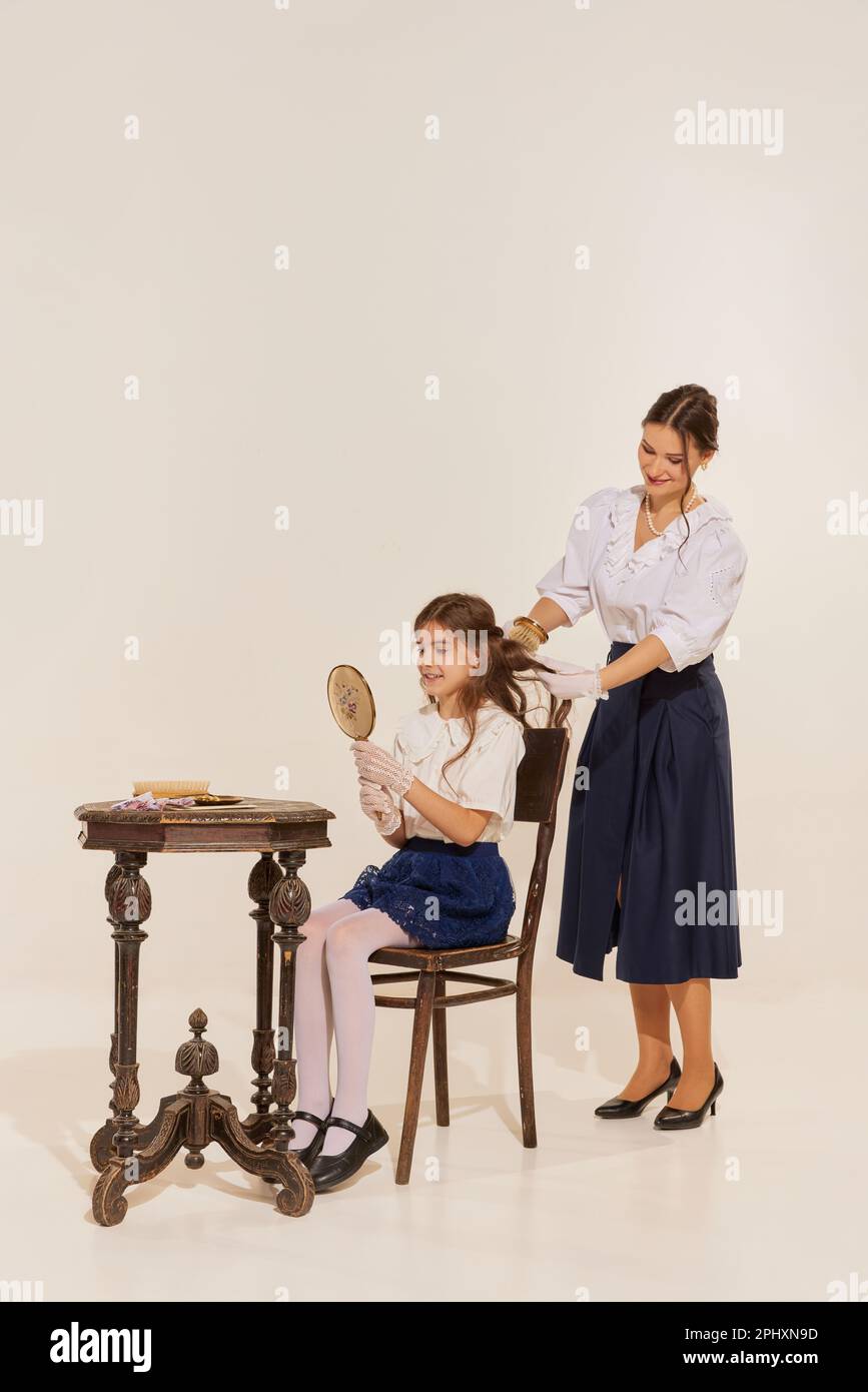 Portrait of young woman wearing old-fashioned clothes braiding daughter ...