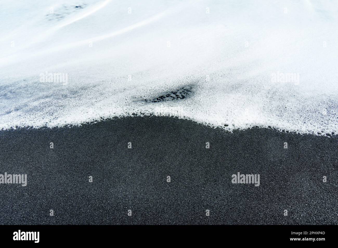 White foamy wave gently covering a black sand beach. Creative peace ...