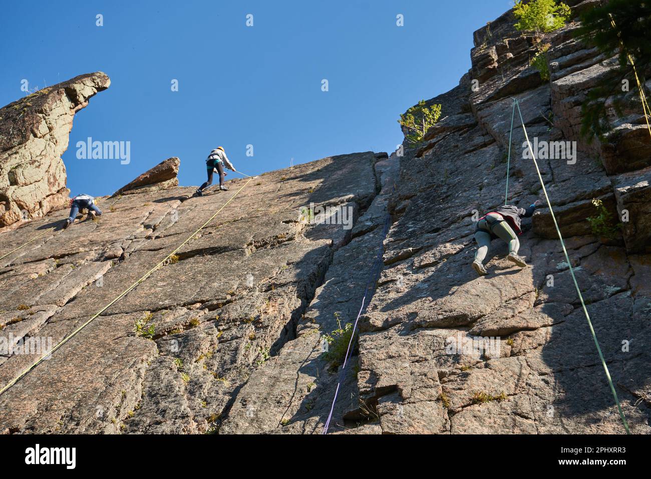 Three climbers in equipment climb up a sheer rock with a top rope on ...