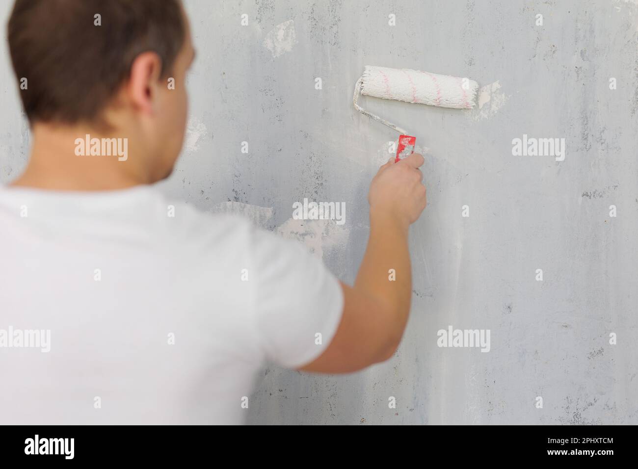 Back view of painter painting grey wall with paint roller Stock Photo ...