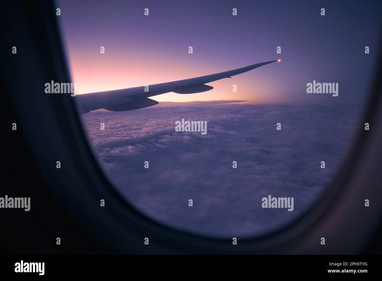 View from window of airplane during flight above clouds at dawn. Selective focus on aircraft ...
