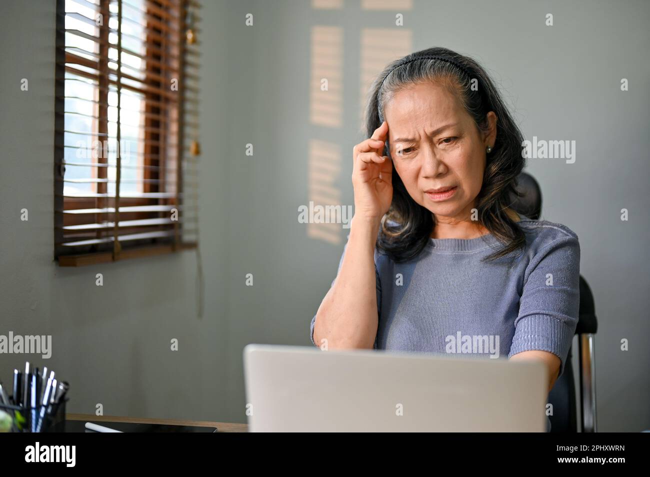 Confused and unhappy Asian-aged woman sits at her desk, having a ...