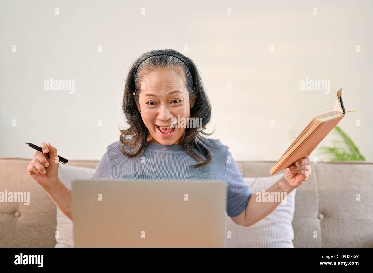 Excited and amazed Asian-aged retired woman holding pen and book, using ...