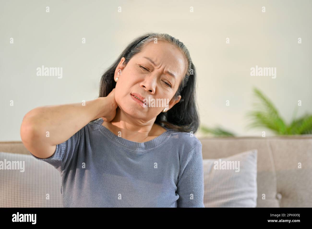 Unhappy senior Asian woman sits on sofa in her living room suffering ...