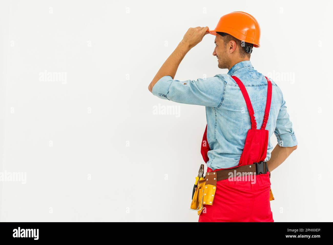 Portrait of cheerful young worker wearing hardhat over white background ...