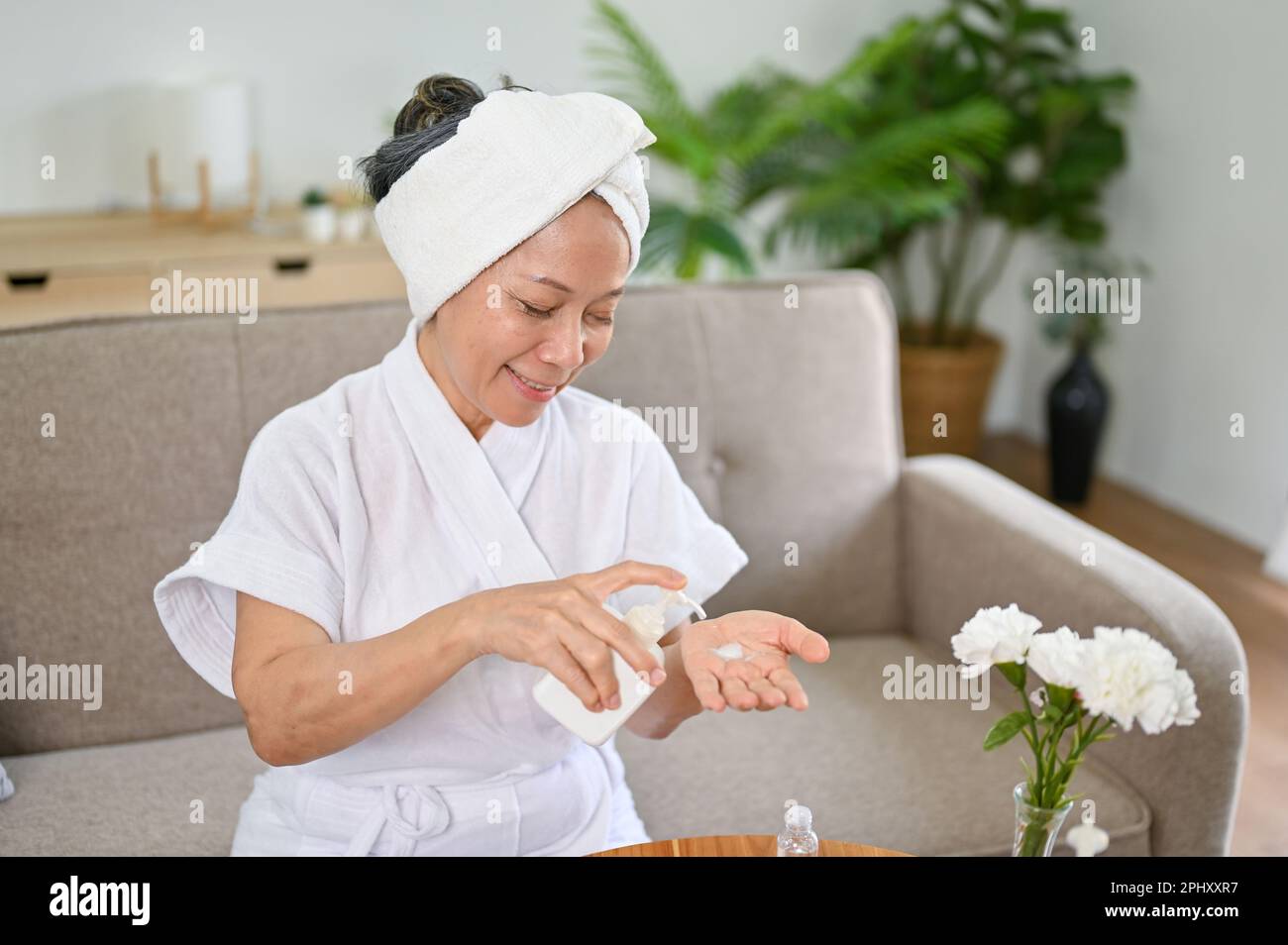 Attractive Asian-aged woman in bathrobe doing her skin care routine ...