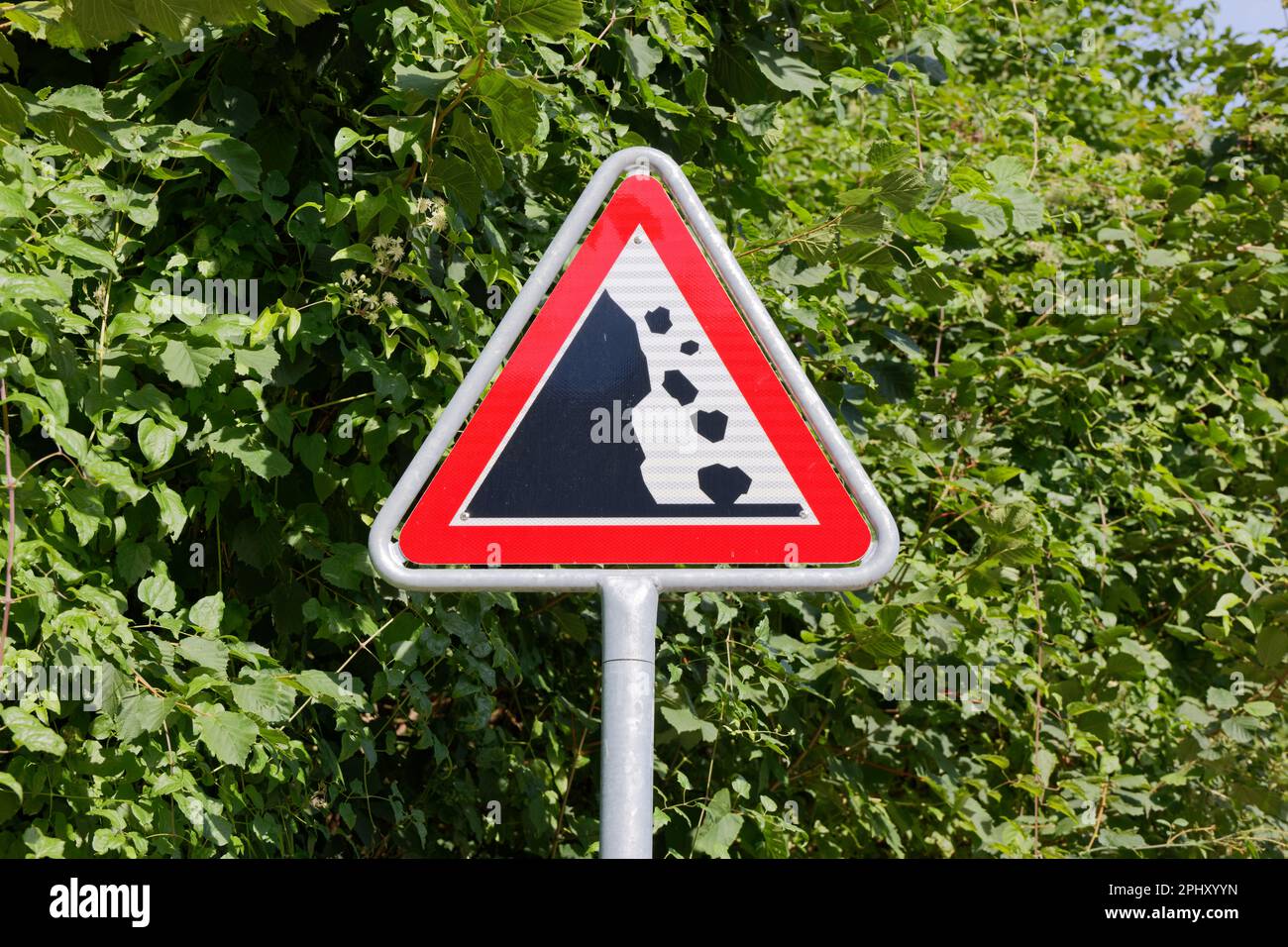 attention falling rocks traffic sign in front of green trees. caution ...