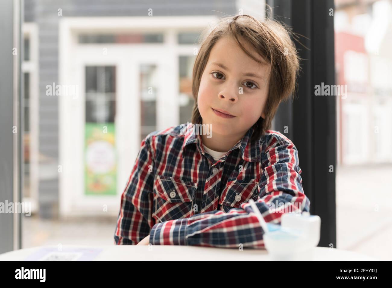 Portrait of cute white boy in a plaid shirt posing in a cafe. Hungry ...