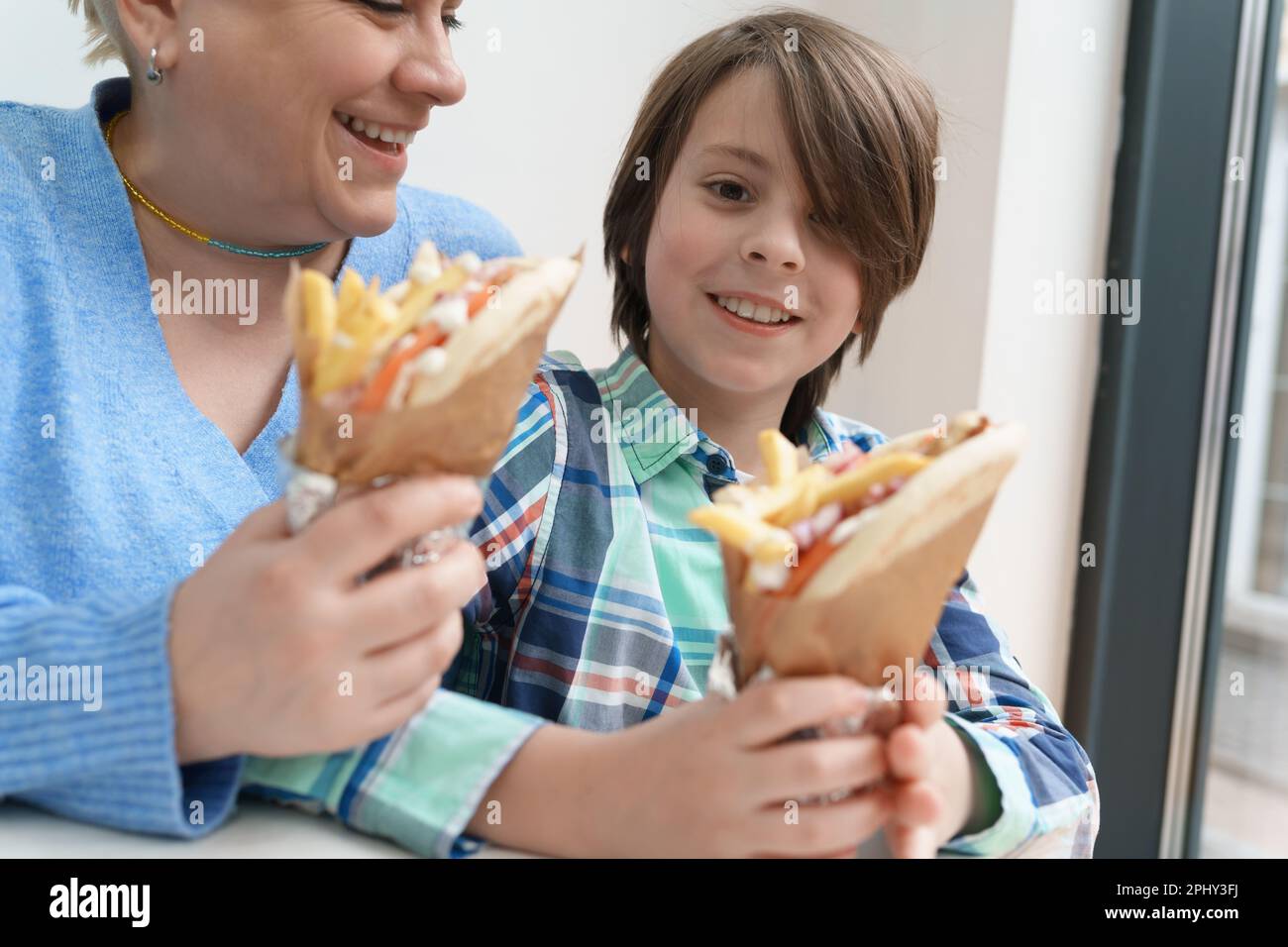 Happy young boy enjoying Greek gyro sandwich together with his mother ...