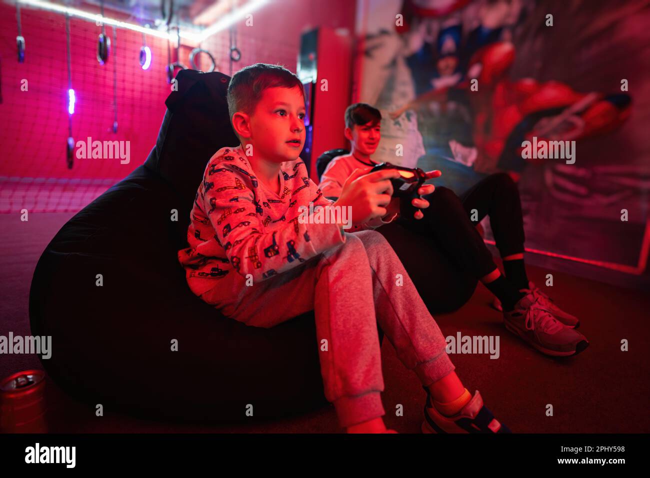 Two boys gamers play gamepad video game console in red gaming room ...