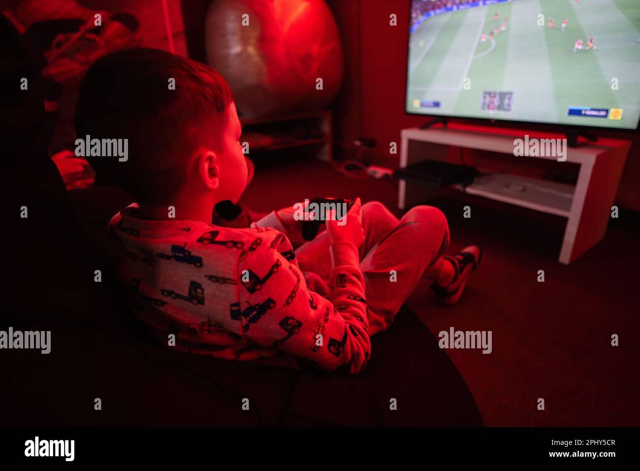 Boy gamer play gamepad football video game console in red gaming room ...