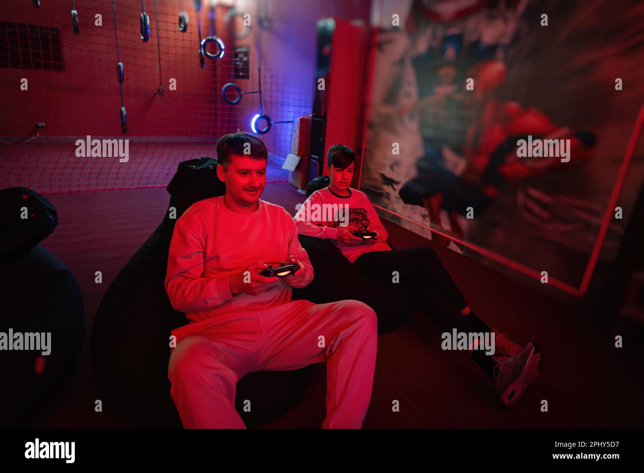 Father and son play gamepad video game console in red gaming room. Dad ...