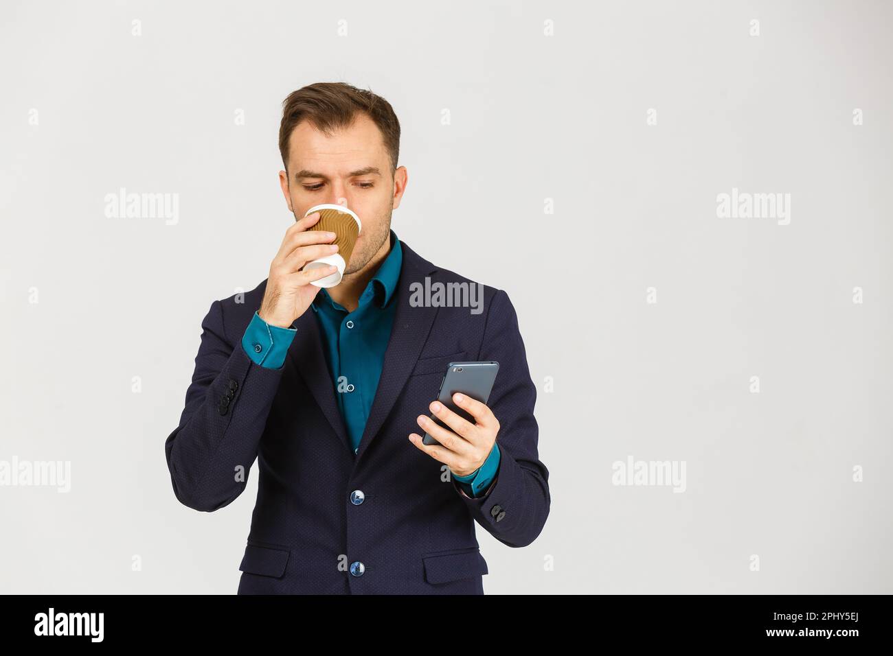 Confident young businessman using cell phone and drinking coffee Stock Photo - Alamy