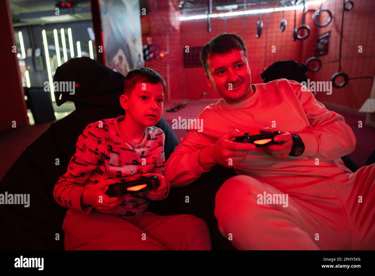 Father and son play gamepad video game console in red gaming room. Dad ...
