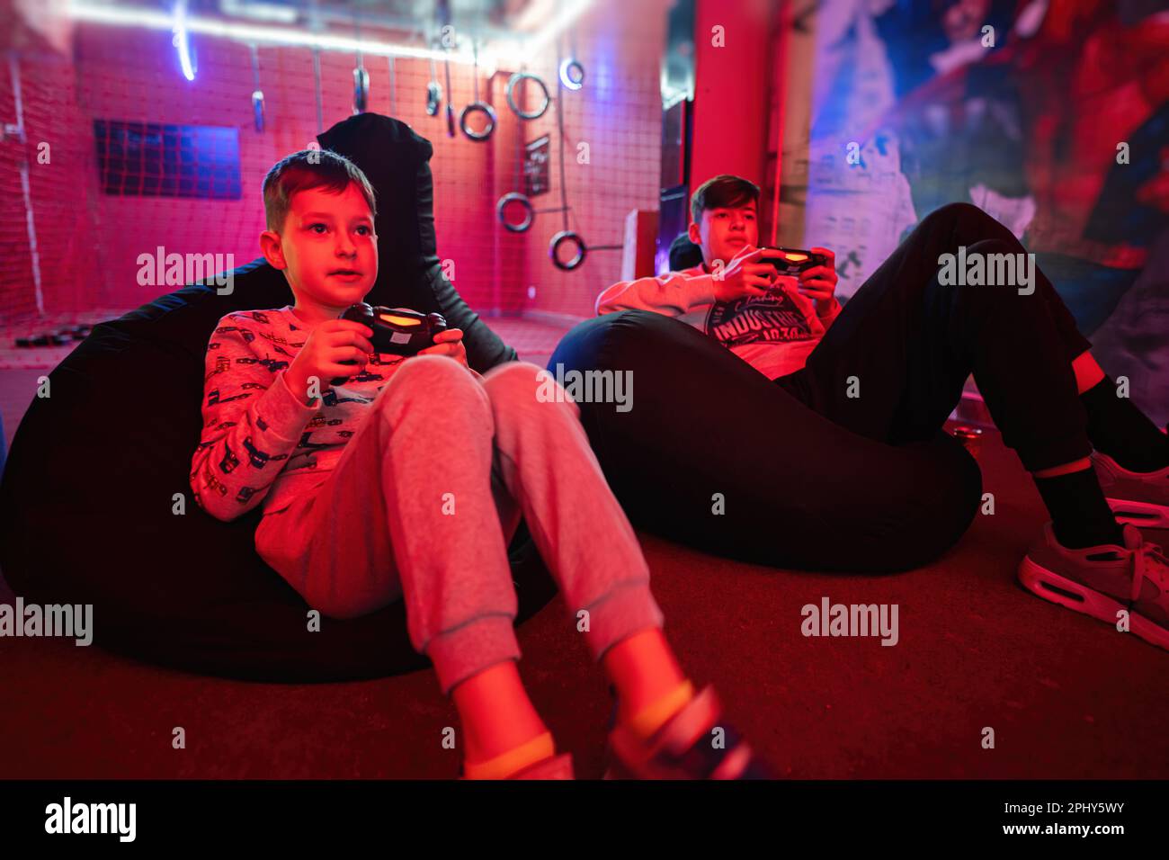 Two boys gamers play gamepad video game console in red gaming room ...