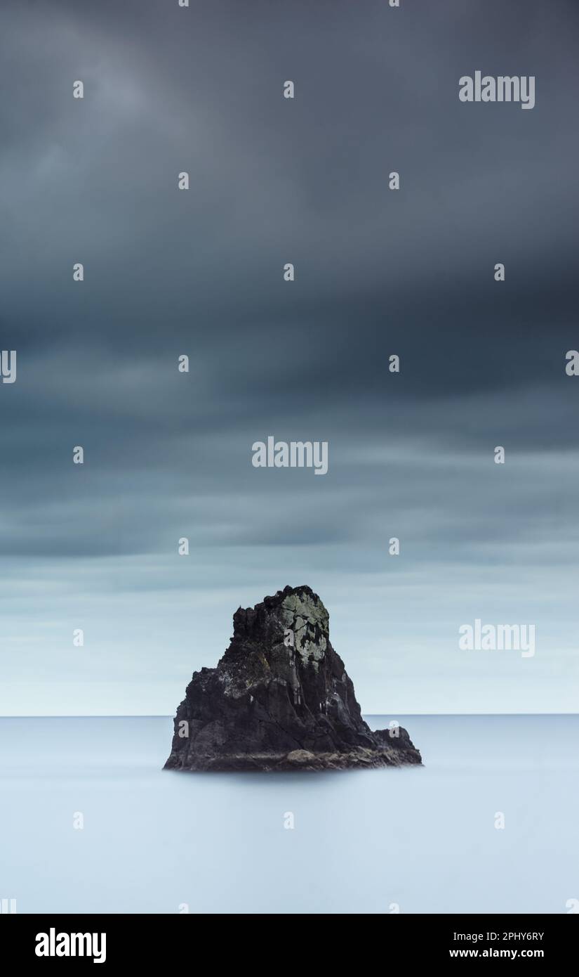 A dramatic sky hangs over the tranquil sea stack, inspiring peace and ...