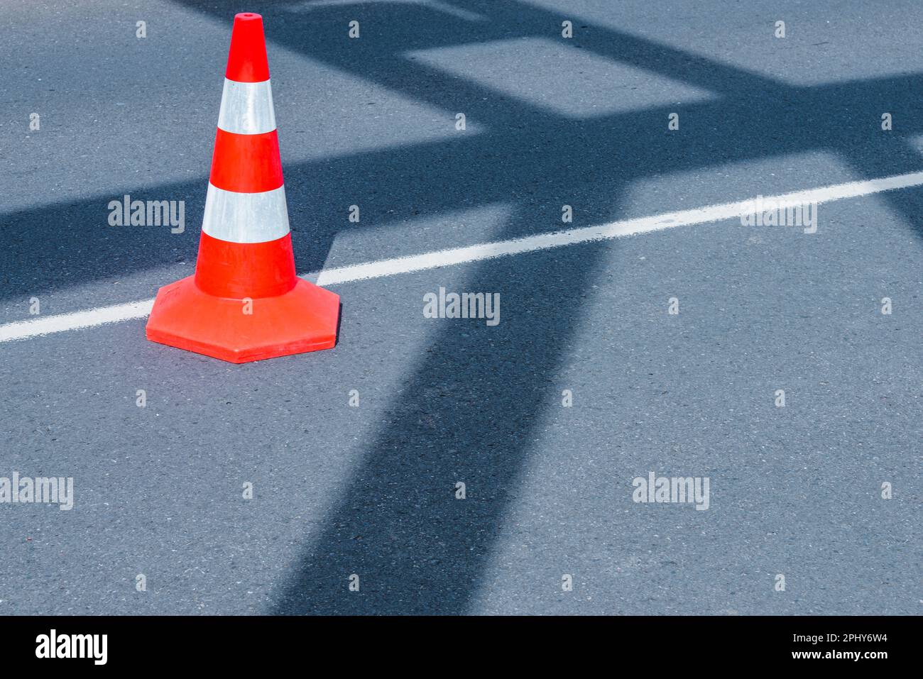 A bright red traffic cone stands alone on an asphalt city street ...