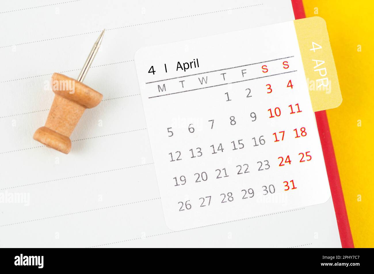 April mini calendar on a white note book with wooden push pin on yellow ...