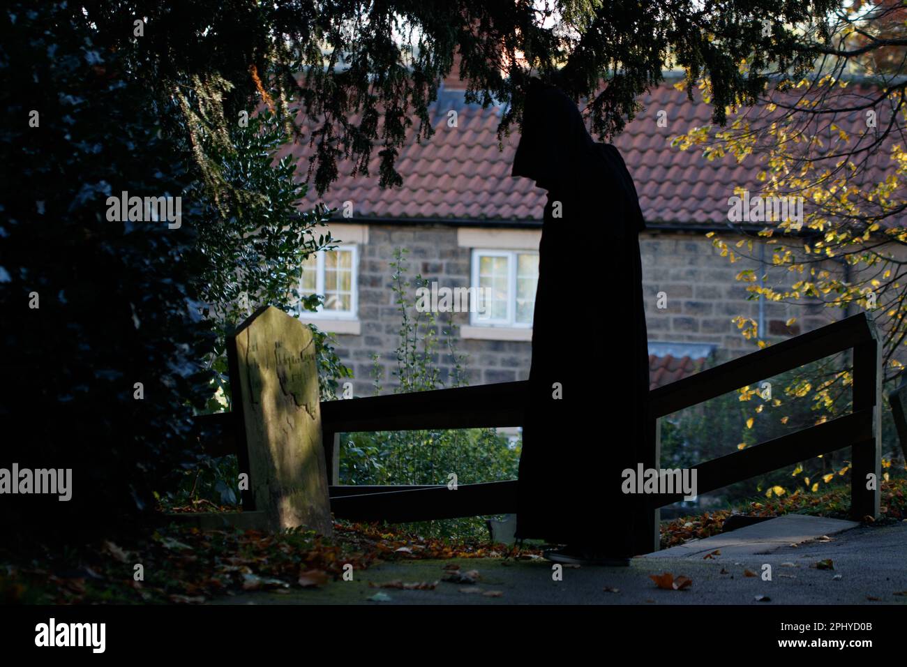 A haunting silhouette of a grim reaper figure standing atop a grave ...