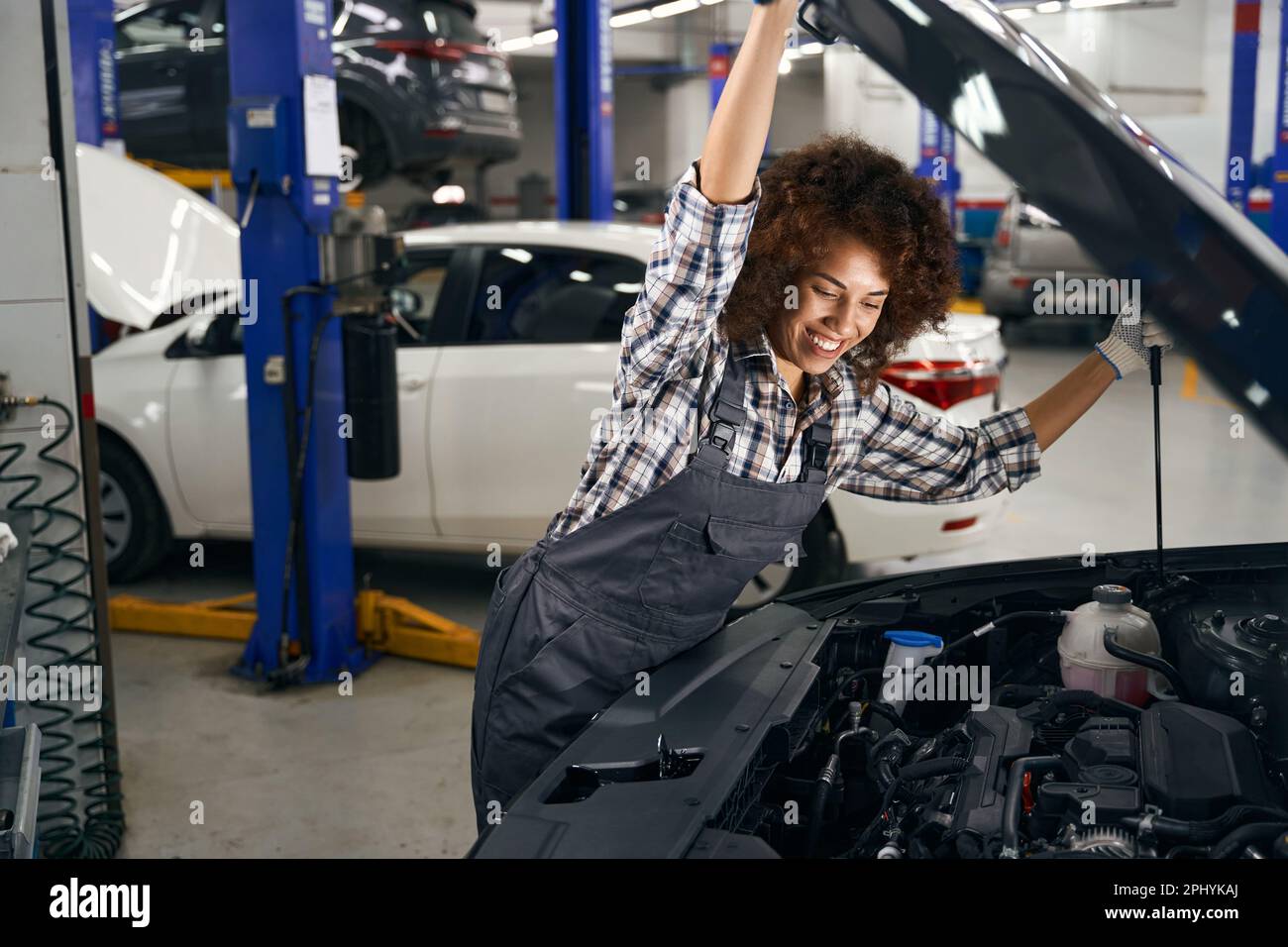 Charming curly car mechanic raises hood top up washer glass Stock Photo ...