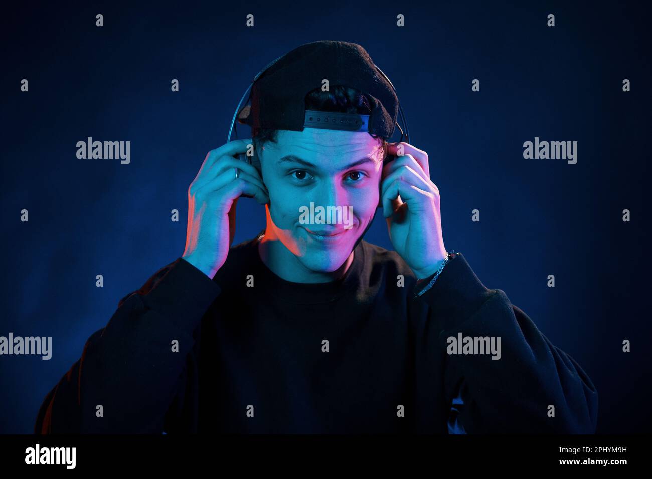 Guy uses headphones. Neon lighting. Young european man is in the dark ...