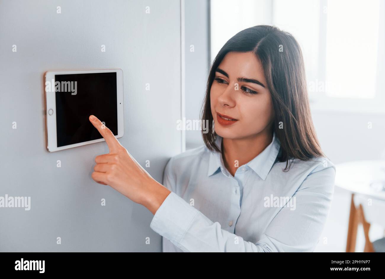 Uses tablet that is mounted in the wall. Young woman is indoors in ...