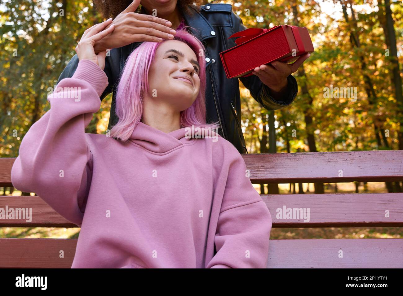Joyous young woman getting present from friend outdoors Stock Photo - Alamy