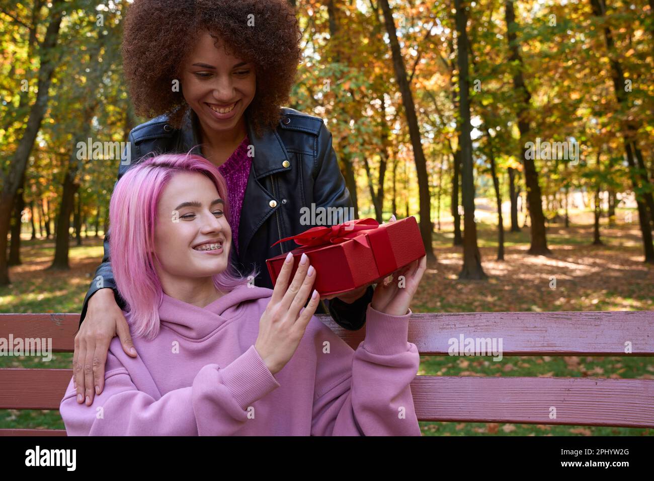 Joyful woman getting birthday present from friend outside Stock Photo ...