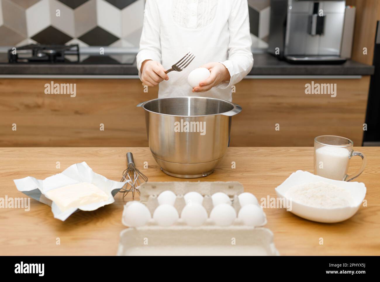 hands of child with no face going to crack egg, preparing and mixing dough in modern kitchen ...