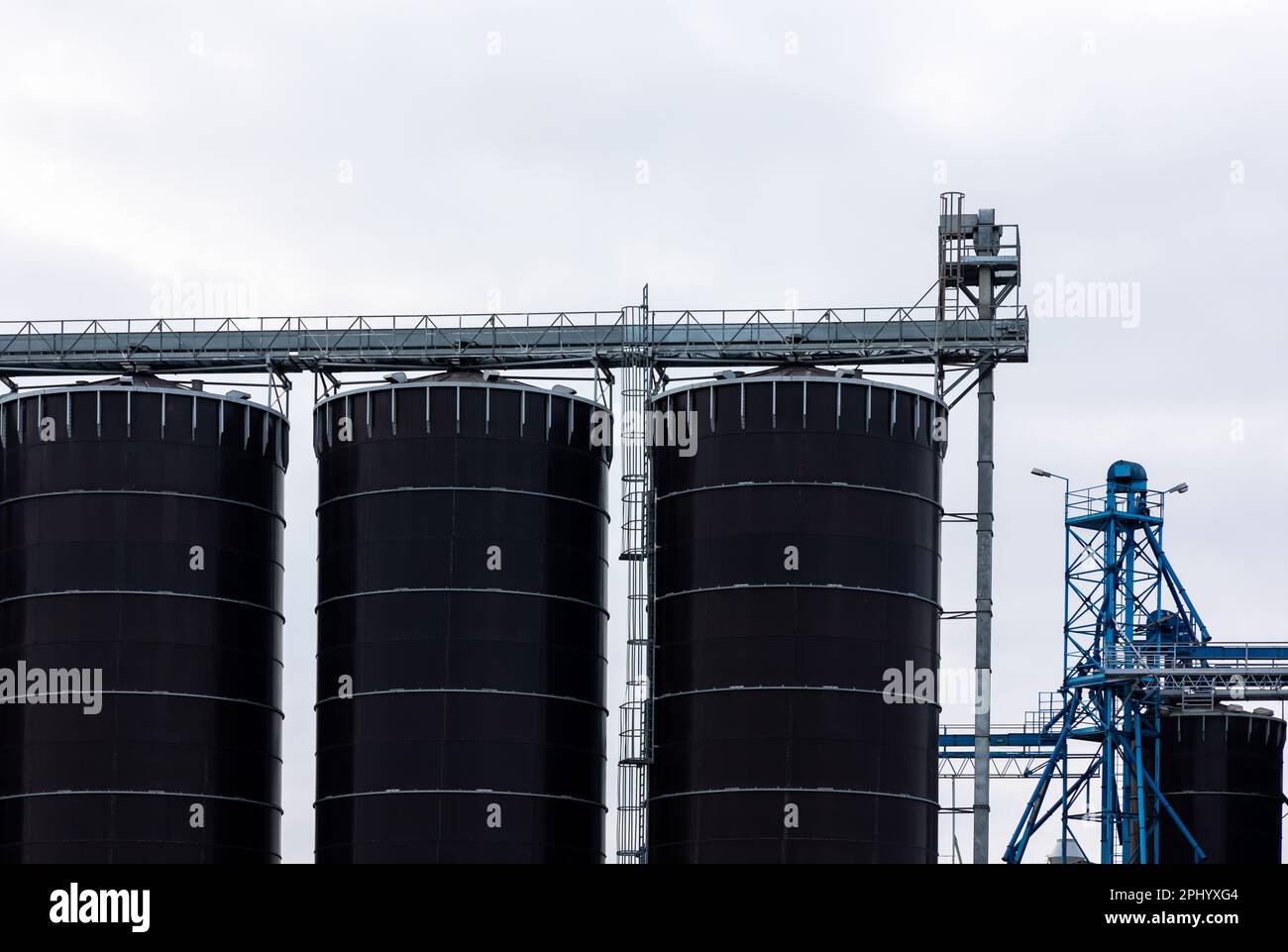 A huge, blackm steel grain silo standing in a field. Warehouses full of ...