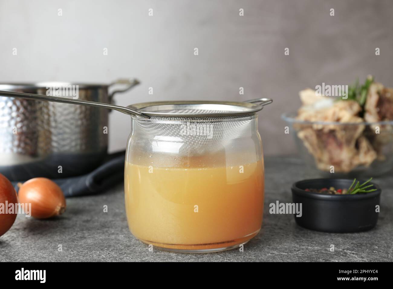 Glass jar with delicious bone broth and sieve on grey table Stock Photo ...