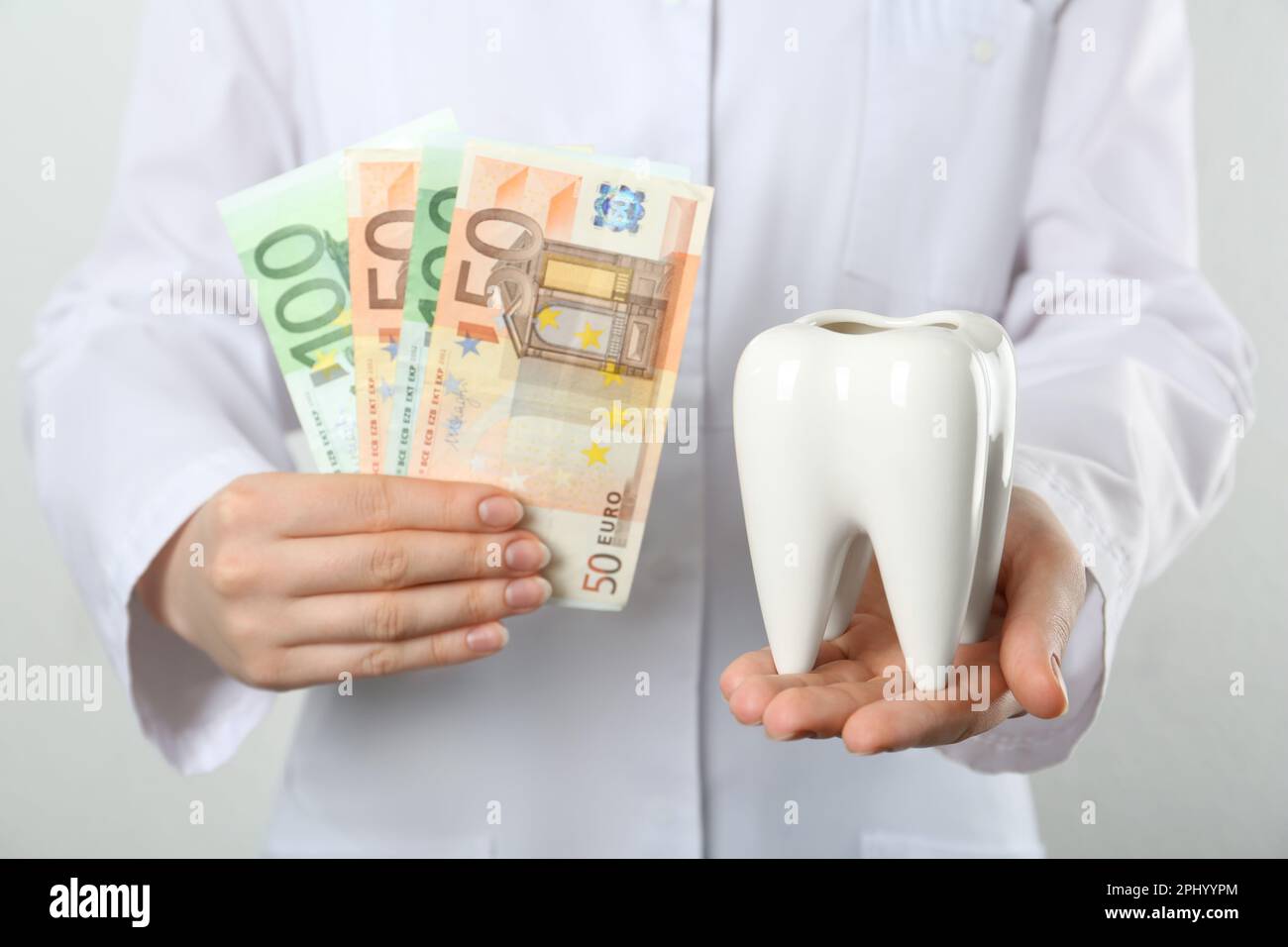 Dentist holding ceramic model of tooth and euro banknotes on light ...