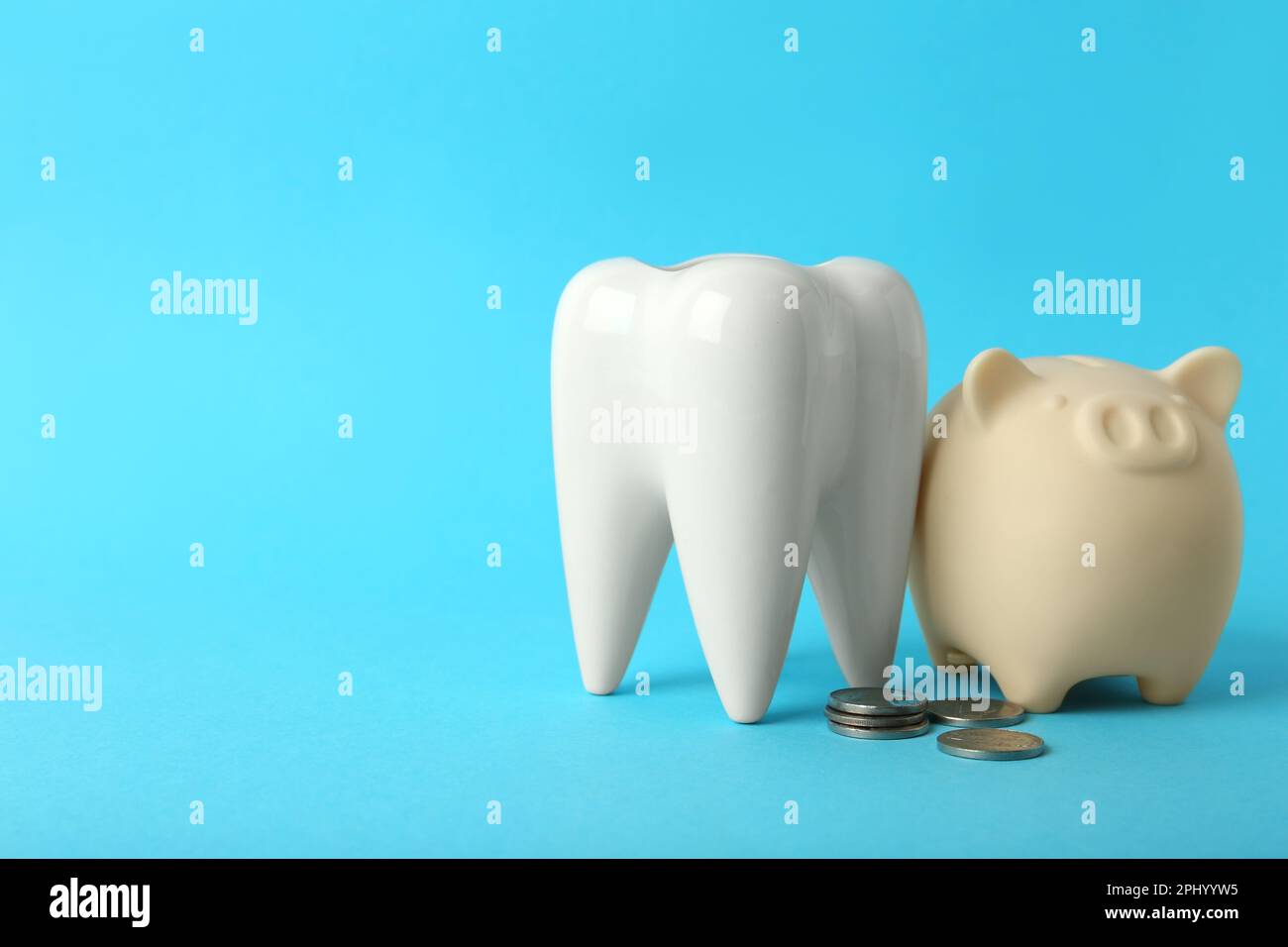 Ceramic model of tooth, piggy bank and coins on light blue background ...