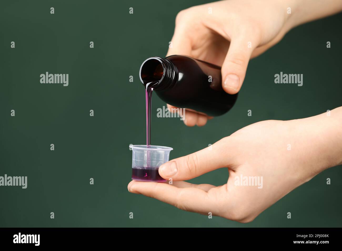 Woman pouring cough syrup into measuring cup on dark green background ...