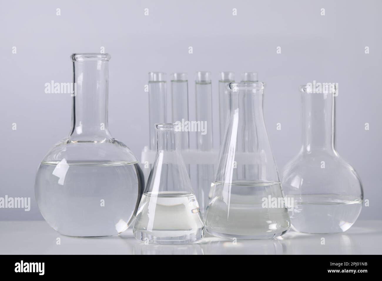 Different laboratory glassware with transparent liquid on table against ...