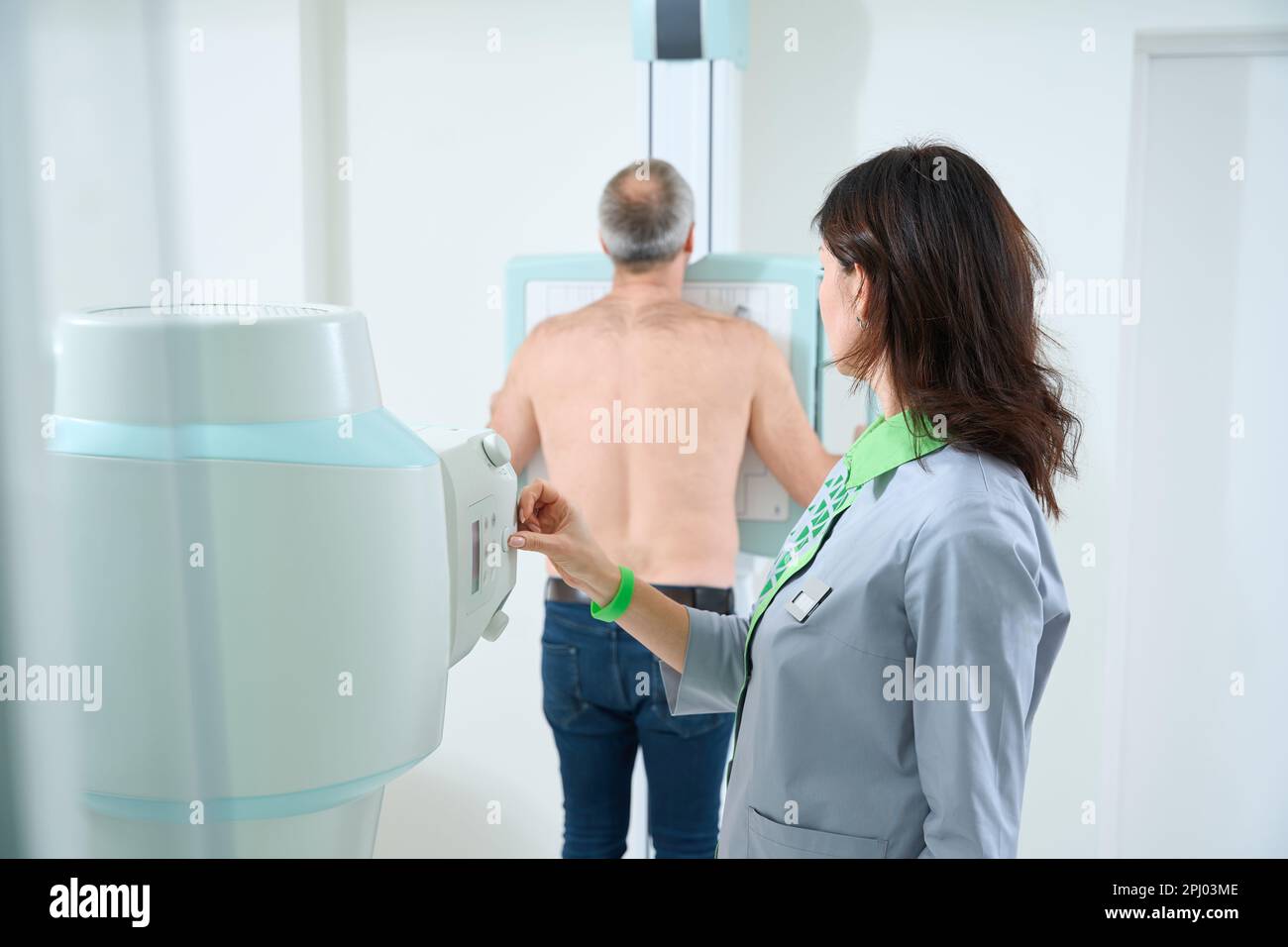 Female doctor adjusting equipment while male patient scanning chest ...
