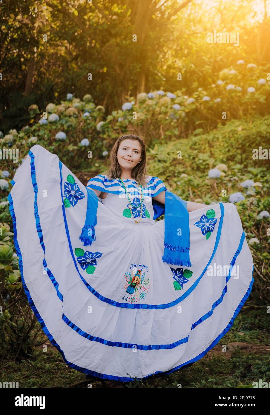 Smiling girl in national folk costume in a field surrounded by flowers ...