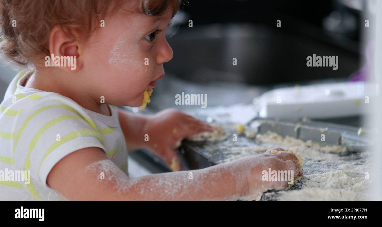 Messy baby child covered with flour at kitchen. Infant one year old ...