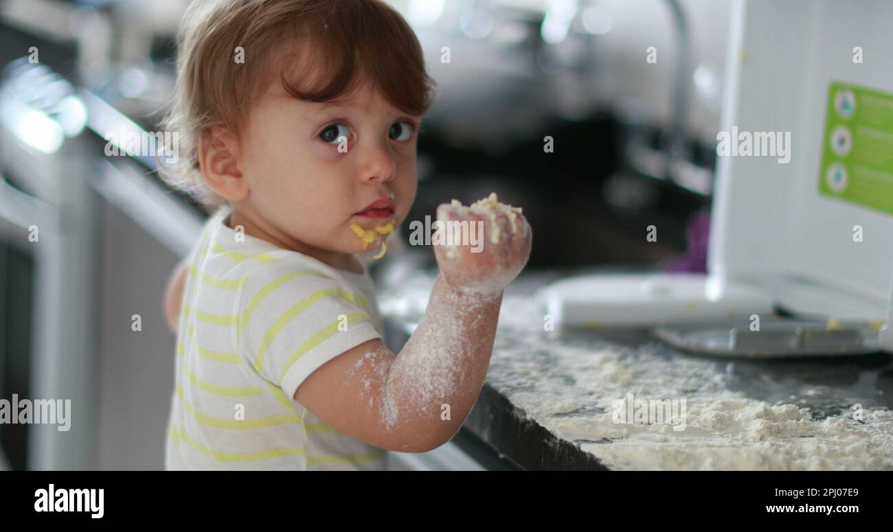 Messy baby playing with flour at kitchen table. One year old child ...
