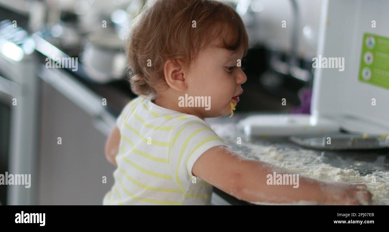 Messy baby playing with flour at kitchen table. One year old child ...