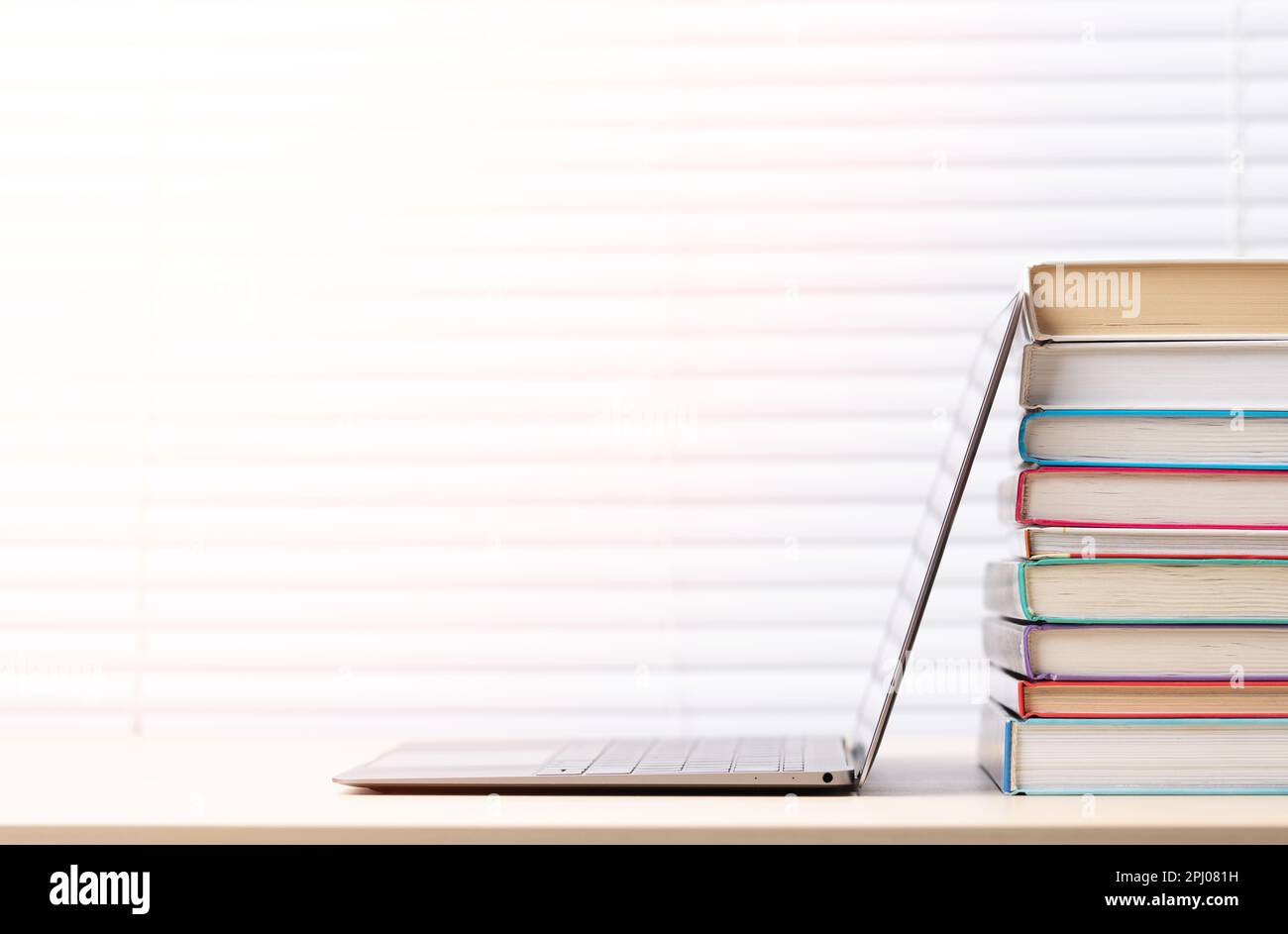 Laptop and stack of books on desk with window blinds in background and ...