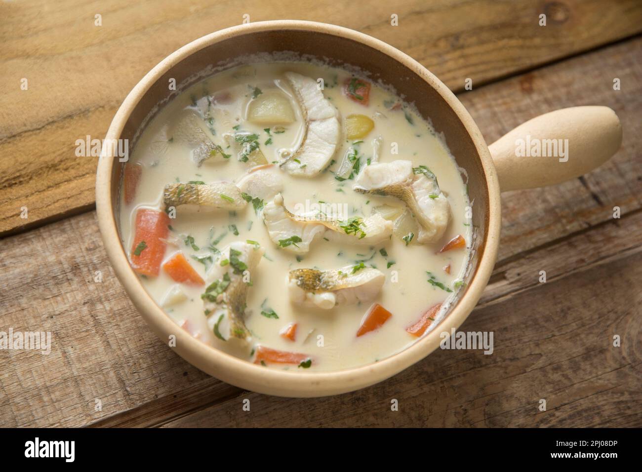 A fish chowder that includes potatoes, carrots and cream with slices ...